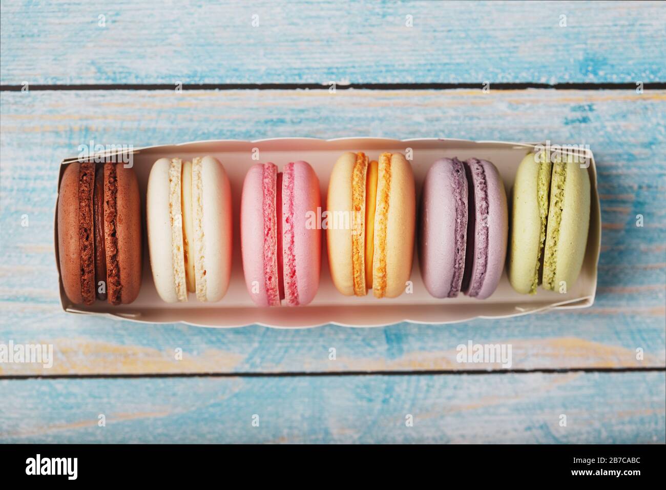 Macaroni cookies of different colors in a box on a blue, old wooden ...
