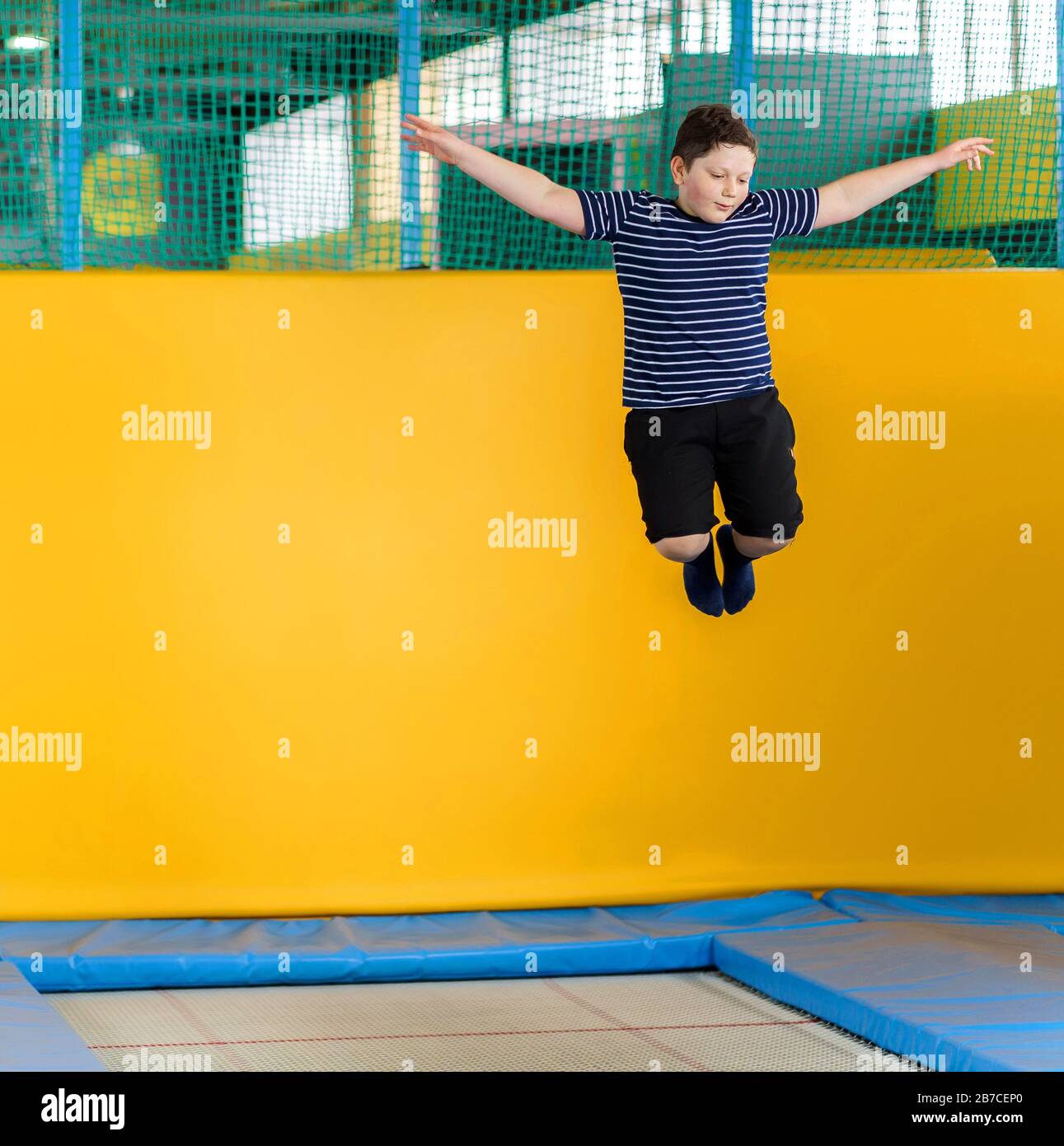 Overweight cute little boy jumping on trampoline indoors in a sport ...