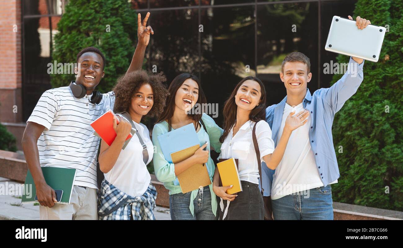 Happy students with workbooks and laptop posing over campus background ...