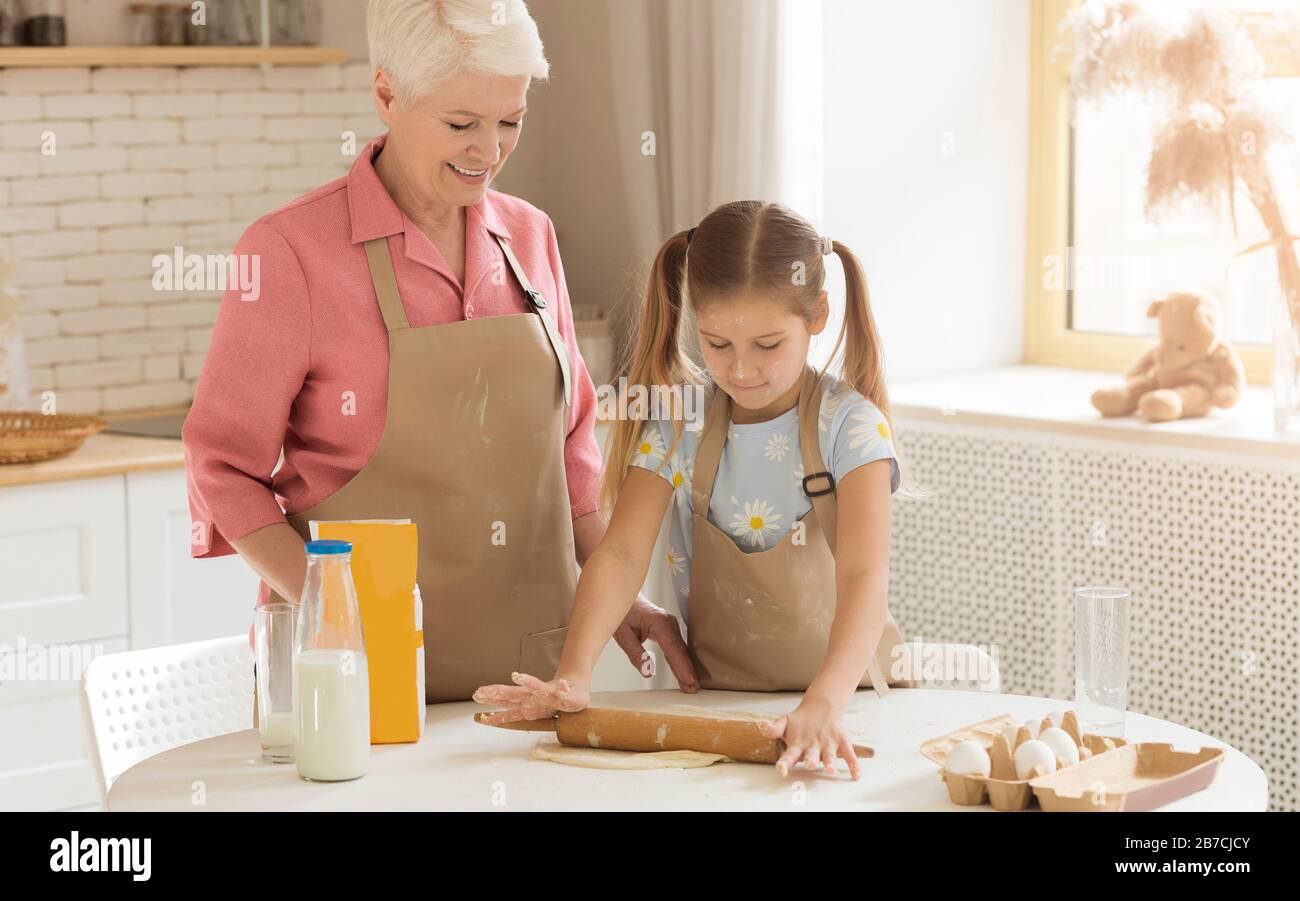 Adorable child learning how to bake from her granny at home Stock Photo ...