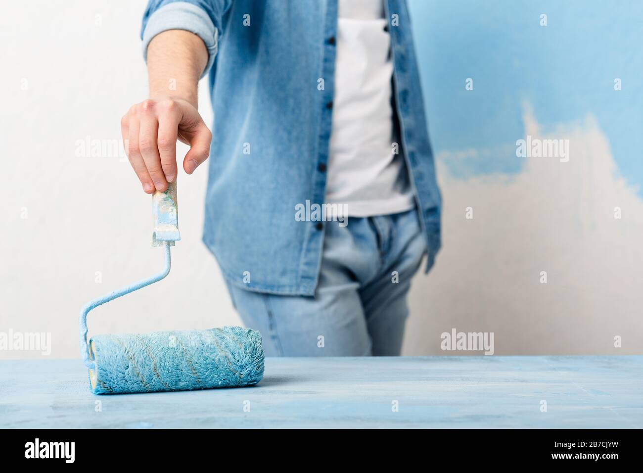 Guy in jeans paints with roller in blue color Stock Photo - Alamy