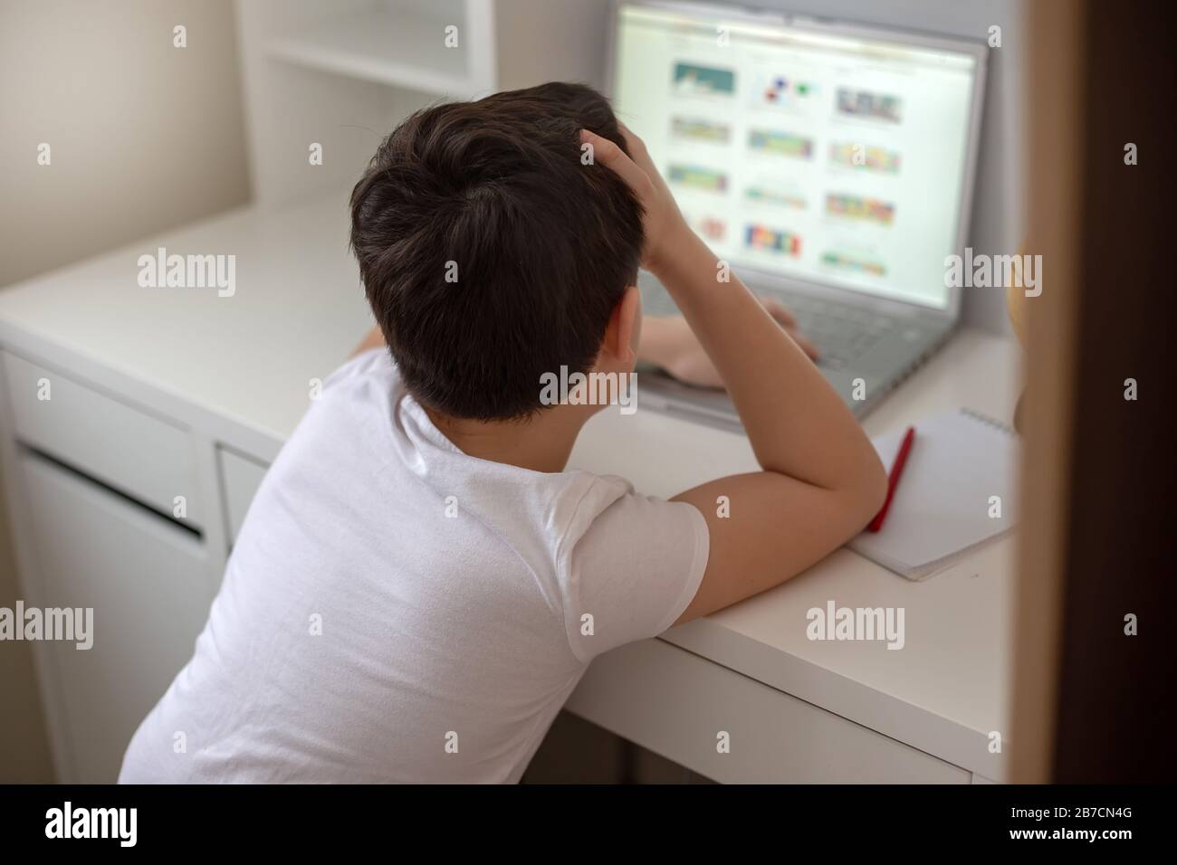 The boy sits with his back behind a laptop, looks on the Internet ...