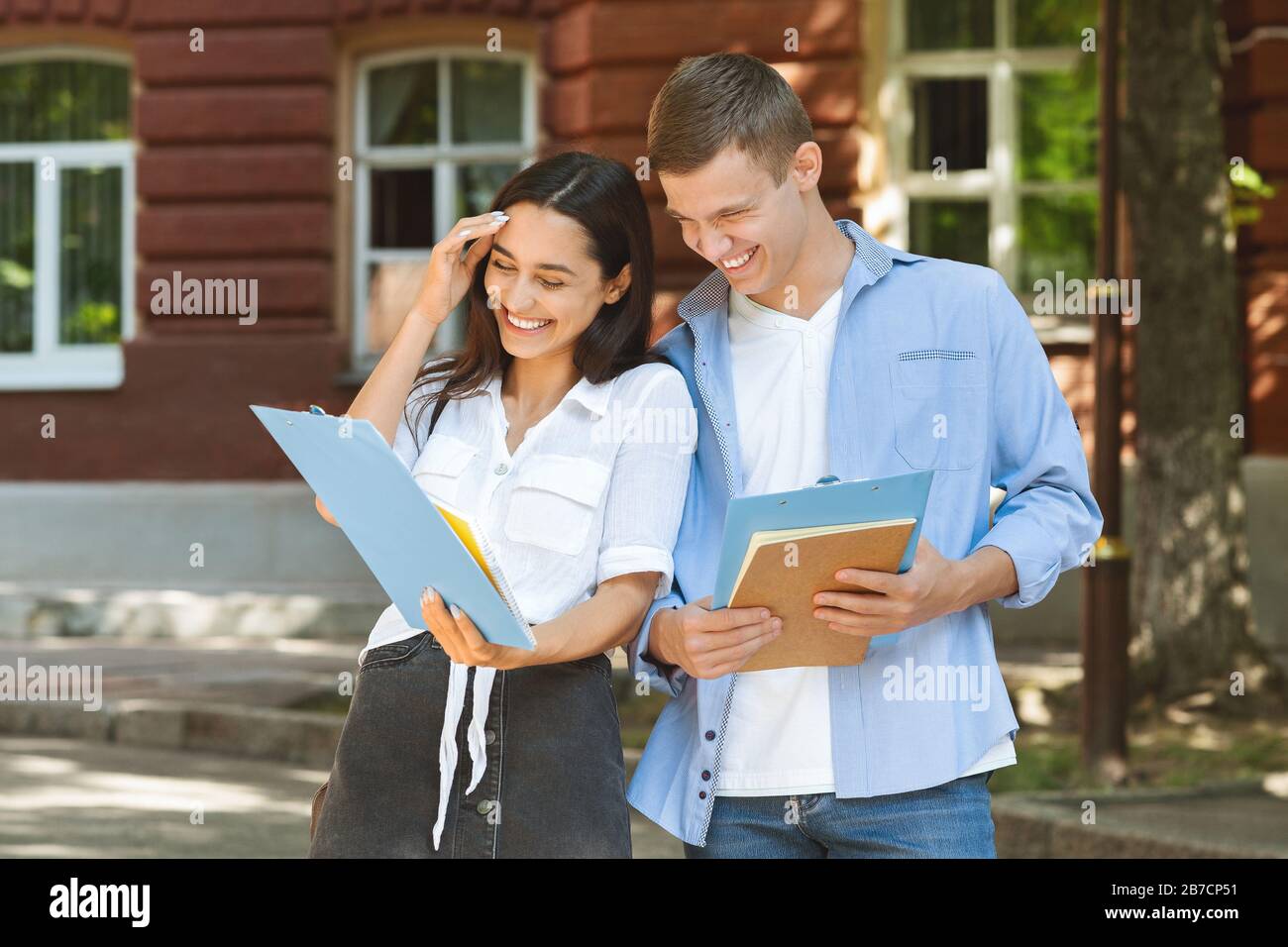 Cheerful couple of university friends laughing outdoors while checking ...