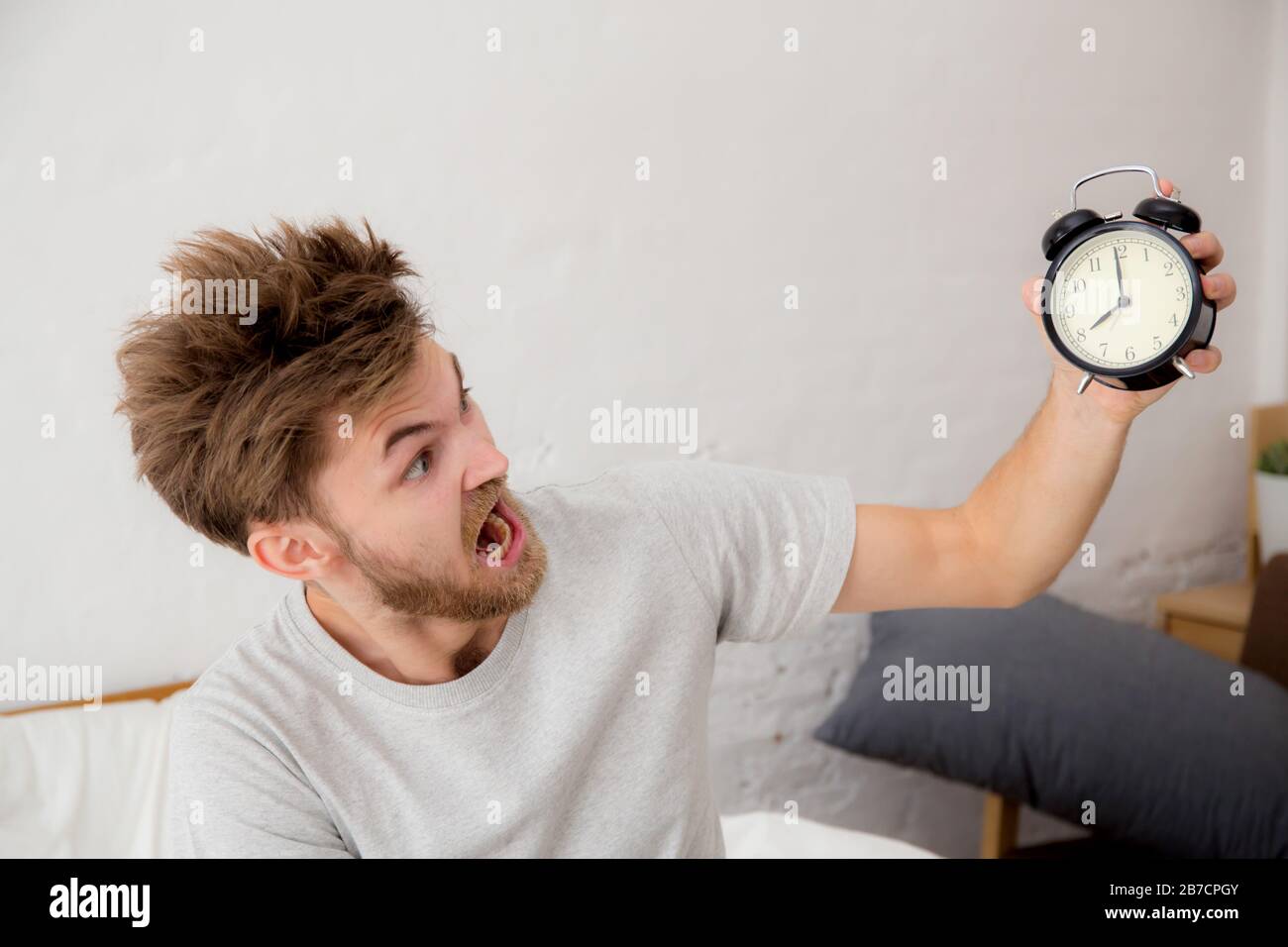Portrait upset angry young man screaming at alarm clock on bedroom ...