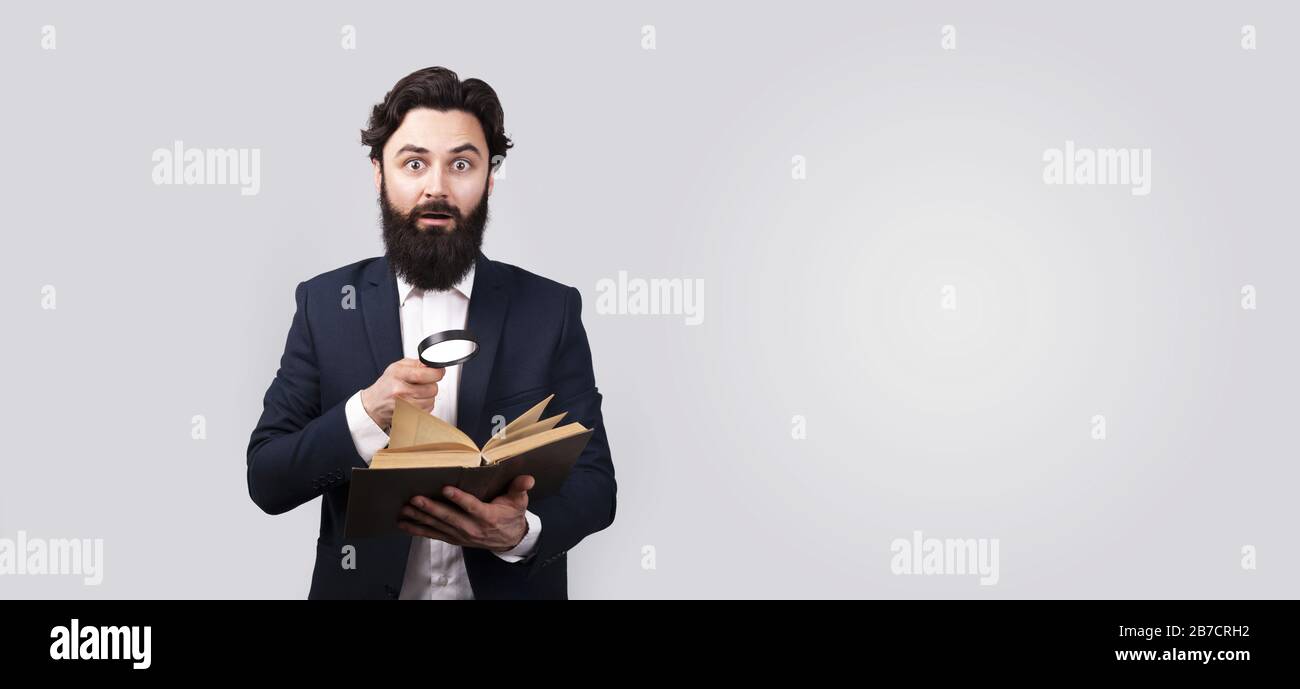shocked bearded man reading book with magnifier, male over gray ...