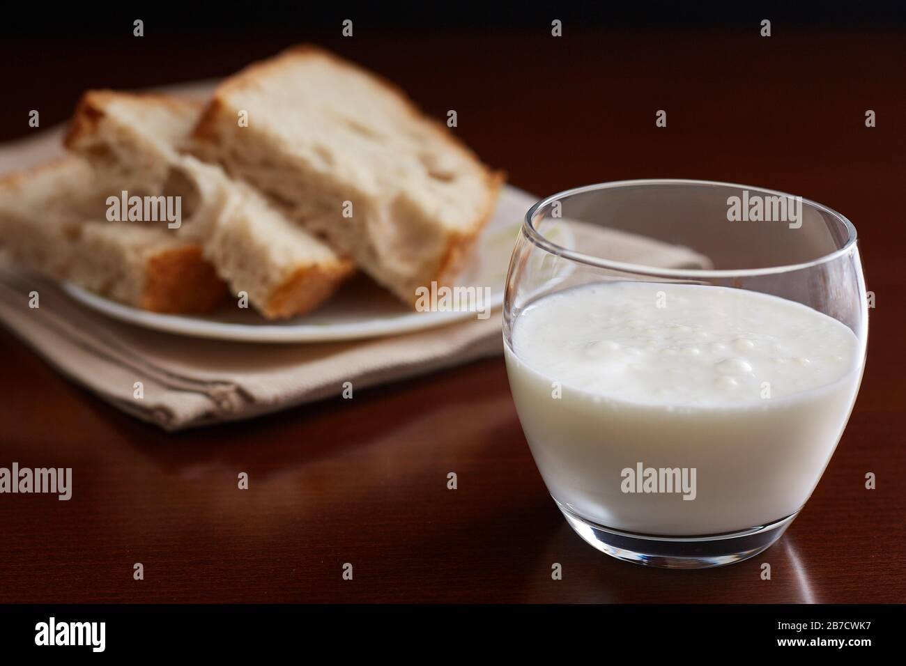 glass cup with kefir on a dark table and background. Handmade bread in ...