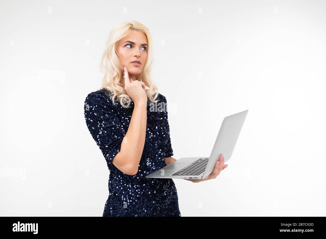 stylish lady in a shiny blue dress holding a laptop and typing on a ...