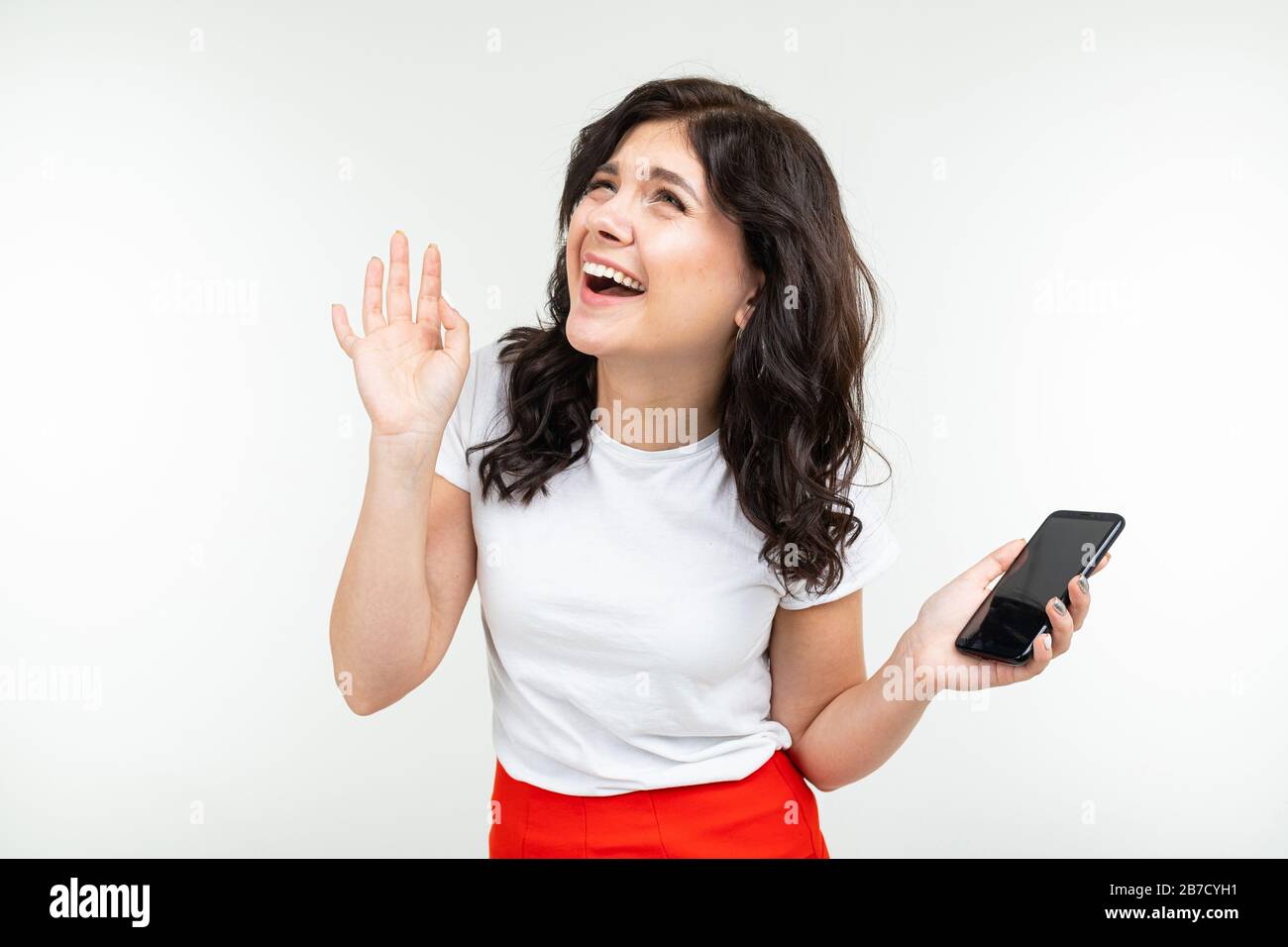 cute girl talking on the speakerphone of a phone on a white studio ...