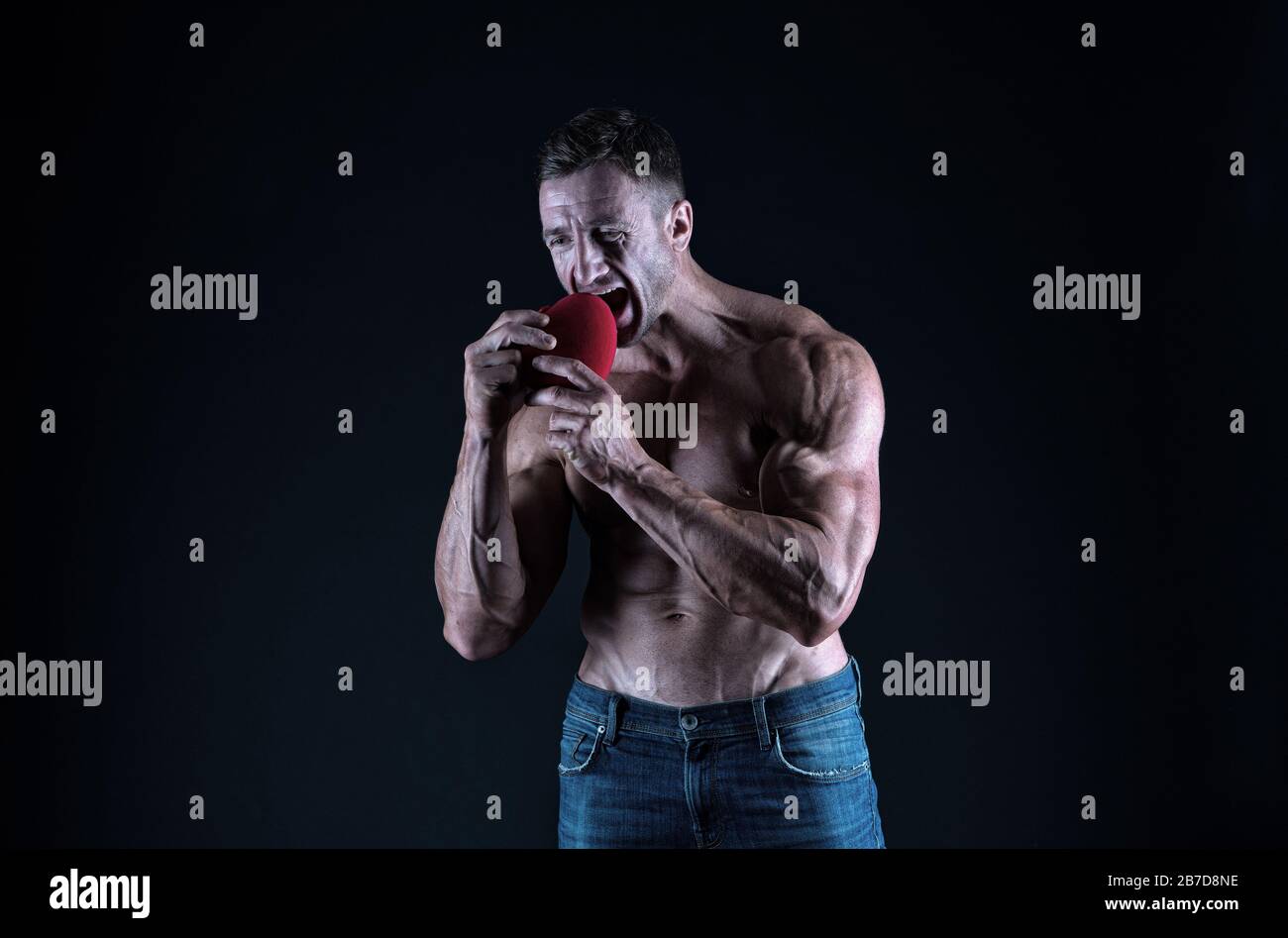 Eating heart healthy diet. Bodybuilder pretend eating red heart ...