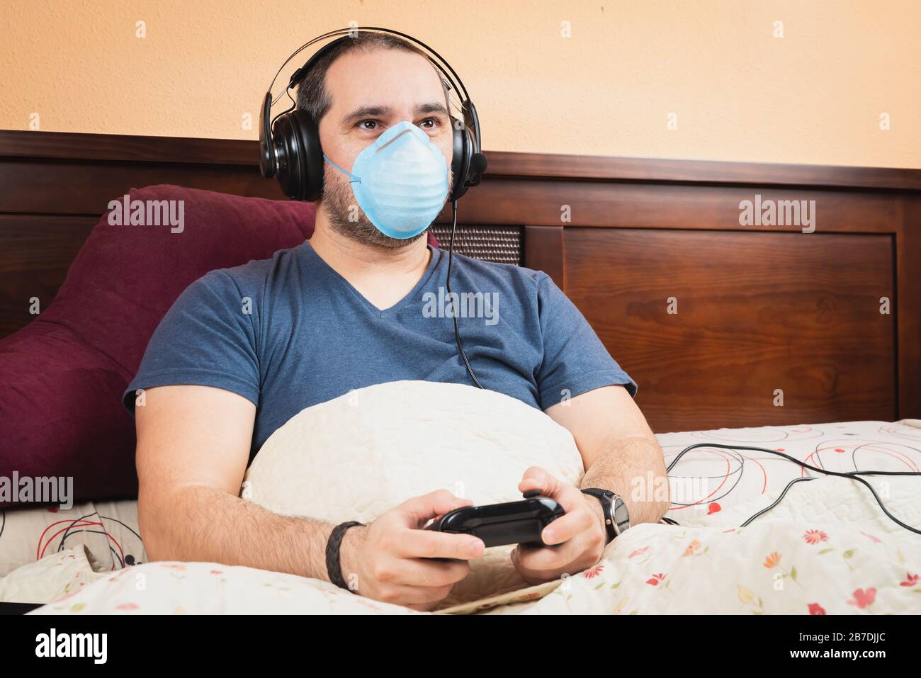 sick man with headphone and medical mask, playing videogames in the bed ...