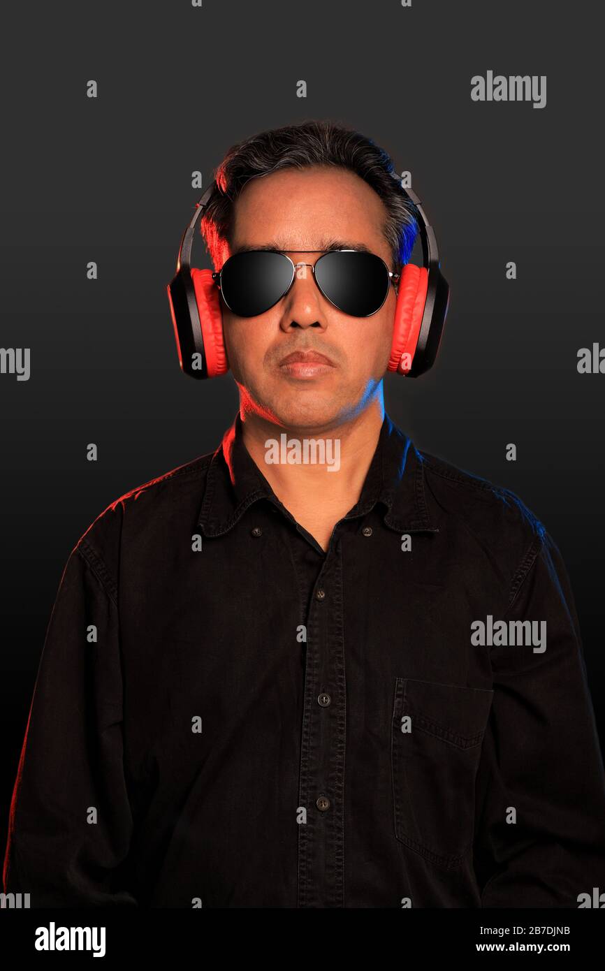 Indian man with sunglasses and wireless headphones on grey background ...