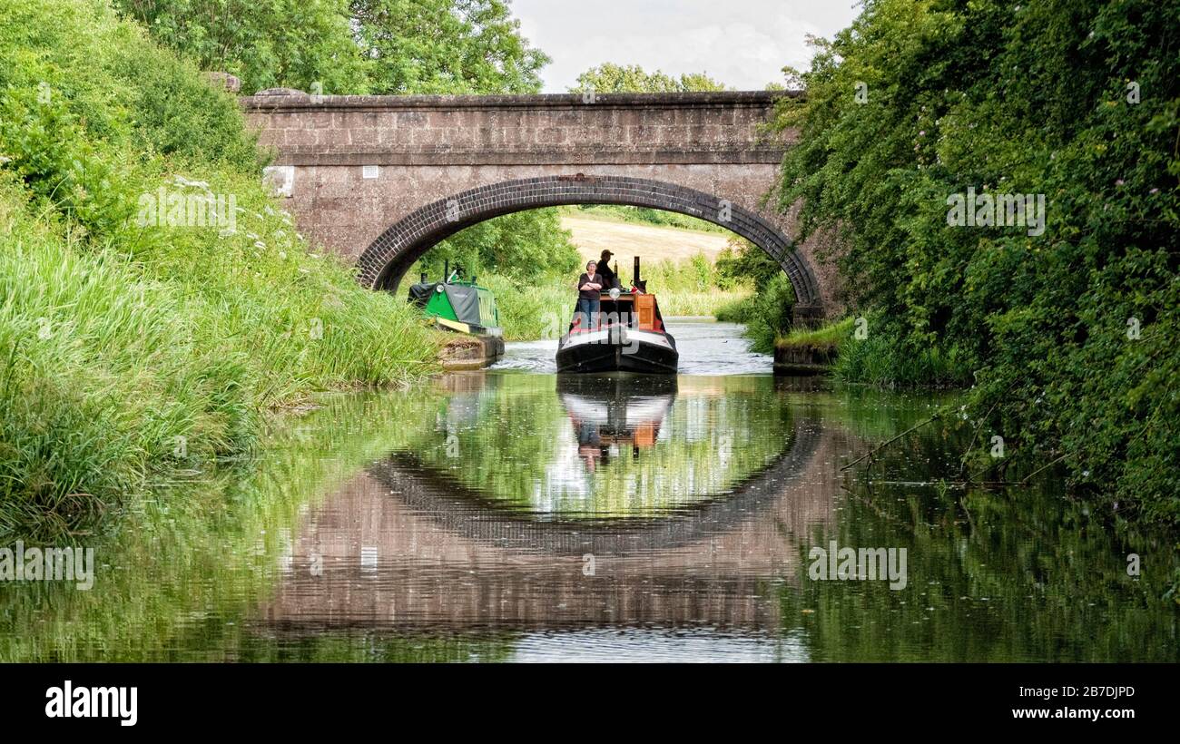 Narrowboat cruising under an arched road bridge on the Grand Union ...