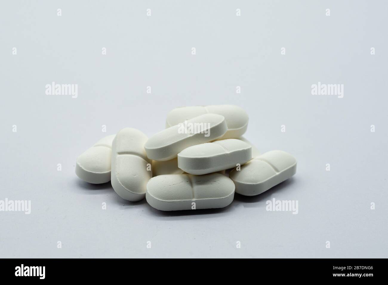 A Number of white medical tablets lying on a white surface and on a ...