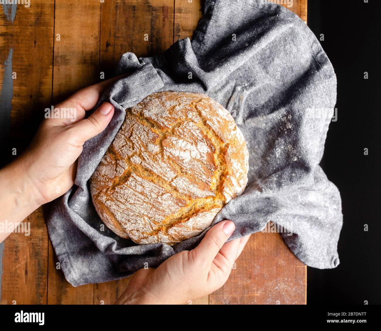 Hands placing a freshly baked loaf of bread wrapped in a grey cloth ...