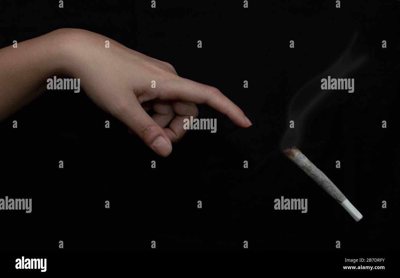 Artistic cannabis background: Hand about to touch a big lit joint of ...