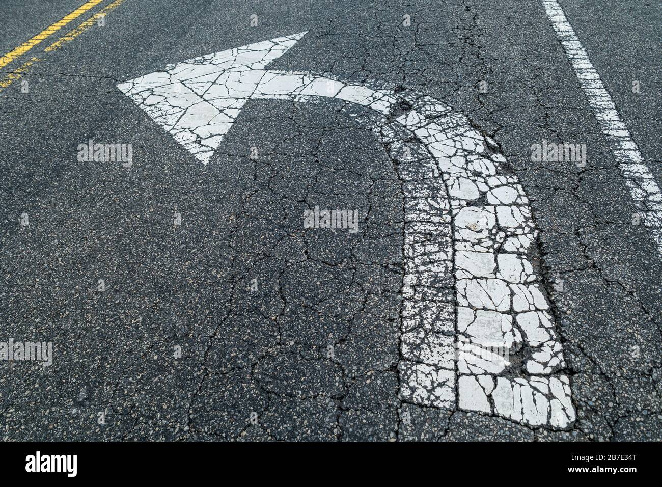 A left turn only arrow painted white on the asphalt cracked and worn ...