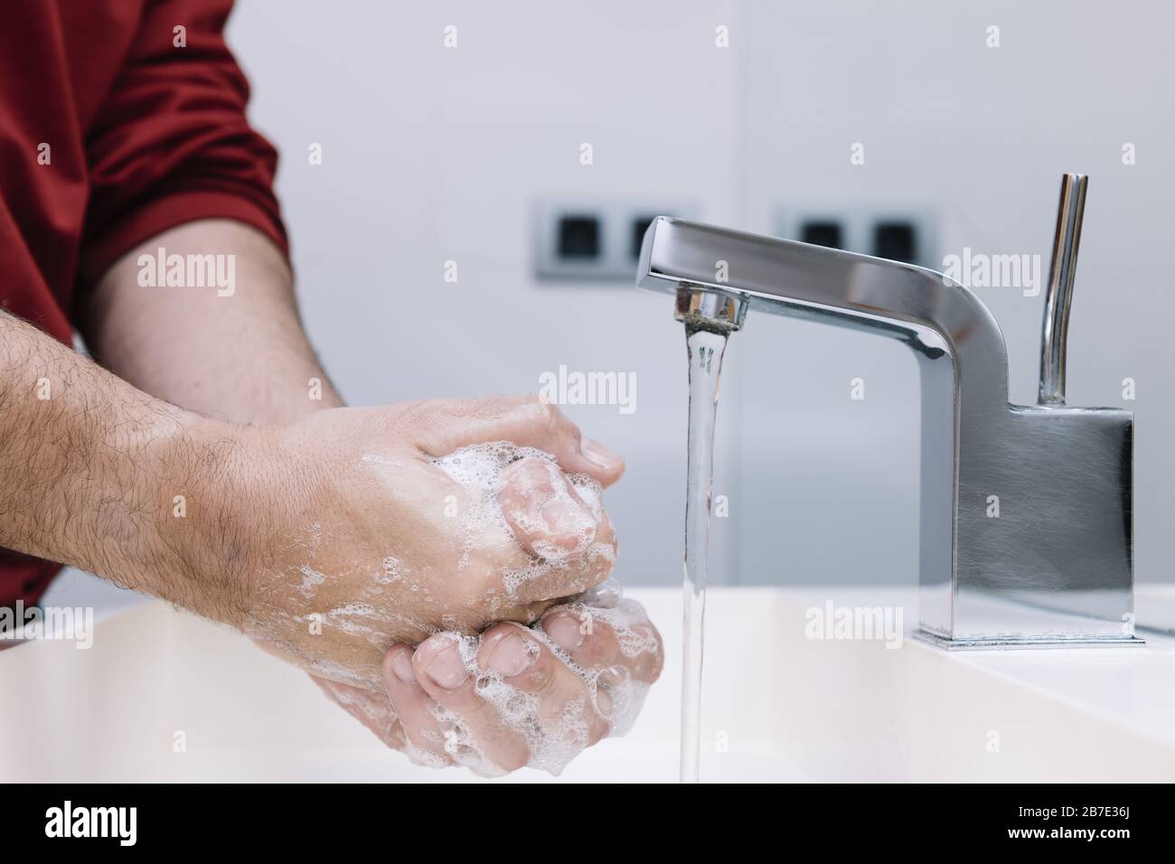 two hands of a man washing in a white modern pile with soap foam and ...