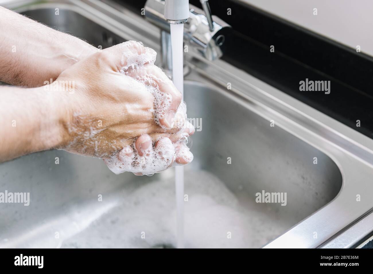 two hands of a man washing in a metallic pile with soap foam and water ...