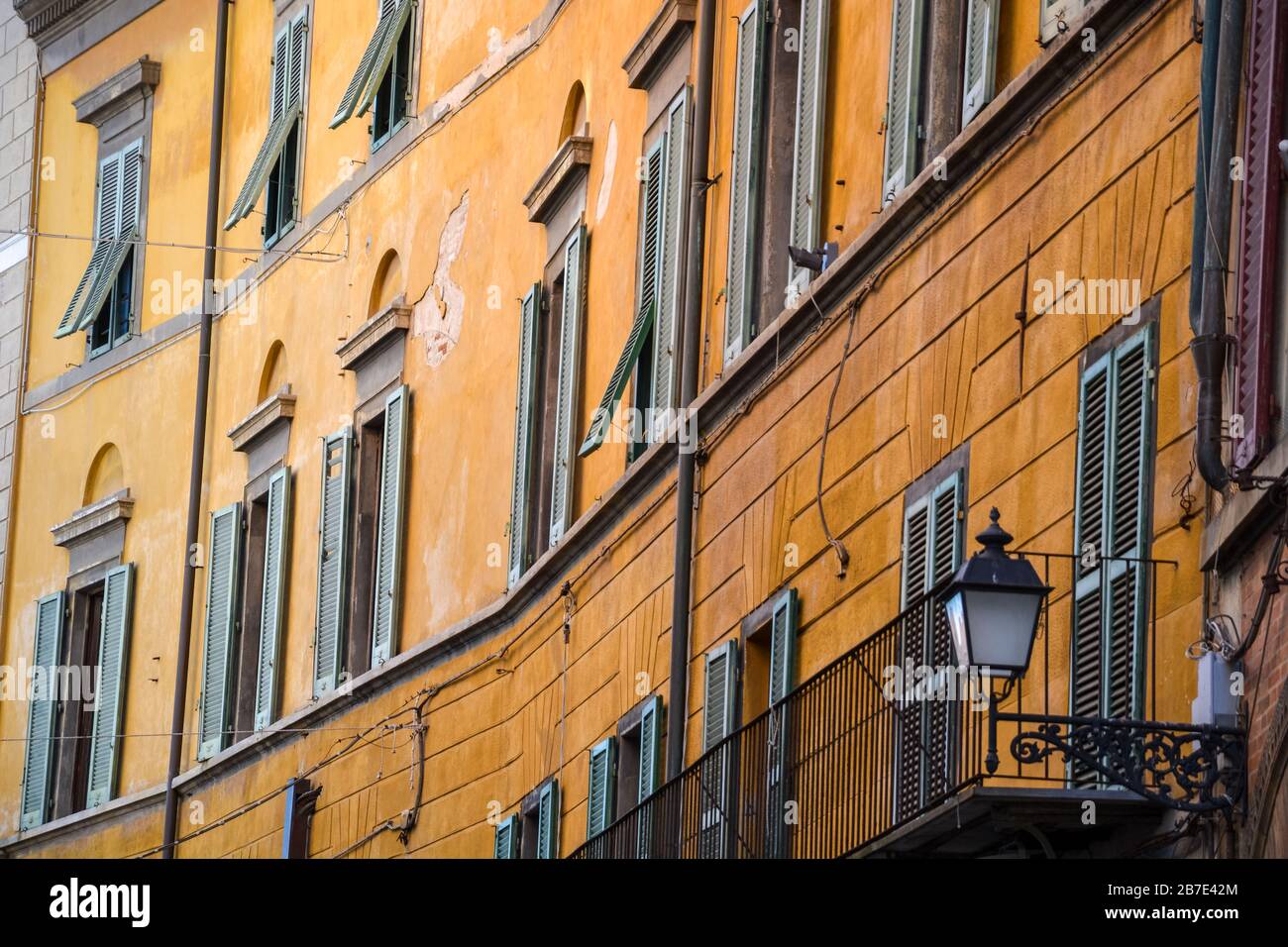 Lots of wooden window frames on an orange wall in Italy from the side ...