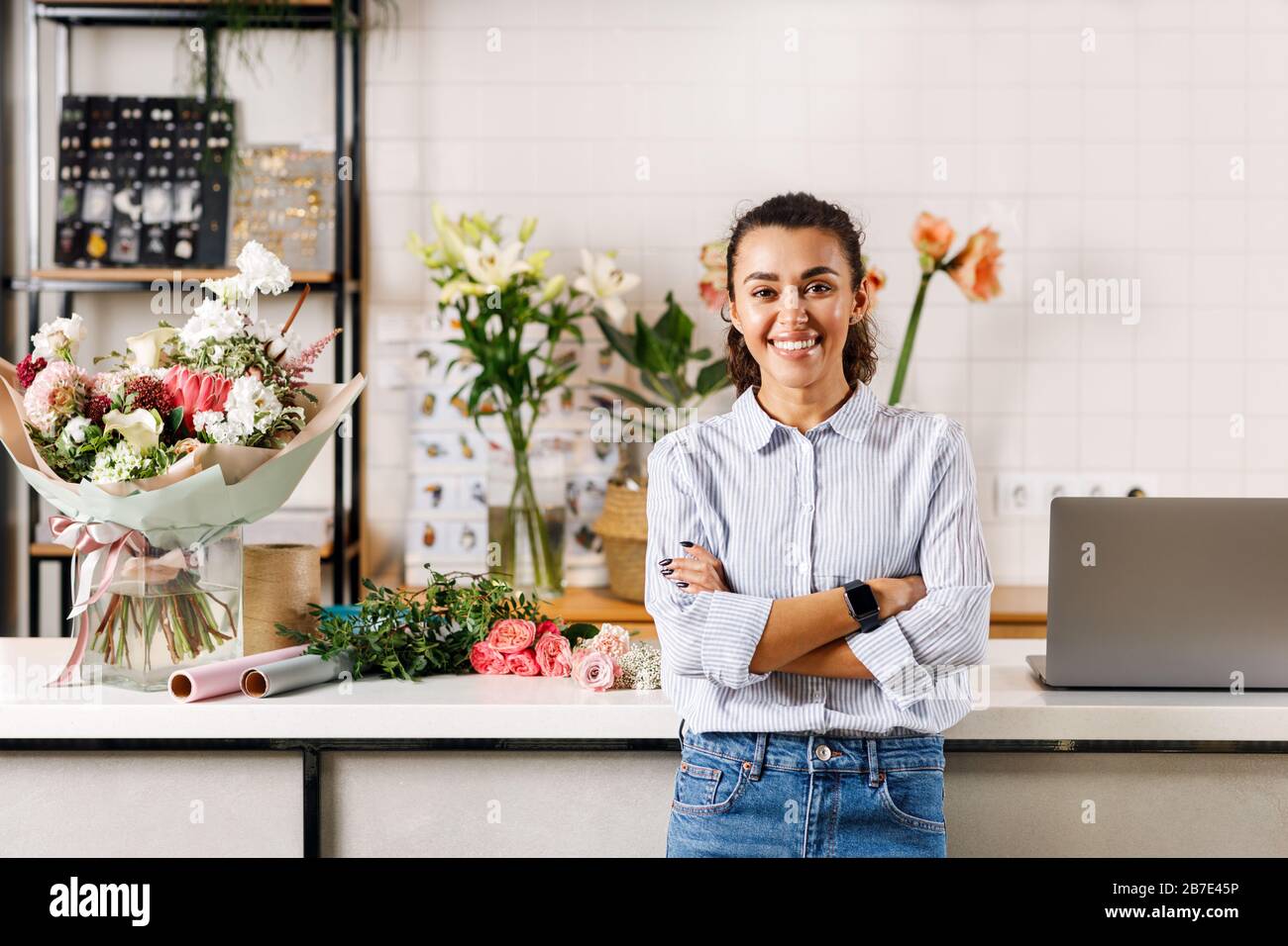 Confident female florist standing with her arms crossed and looking at ...
