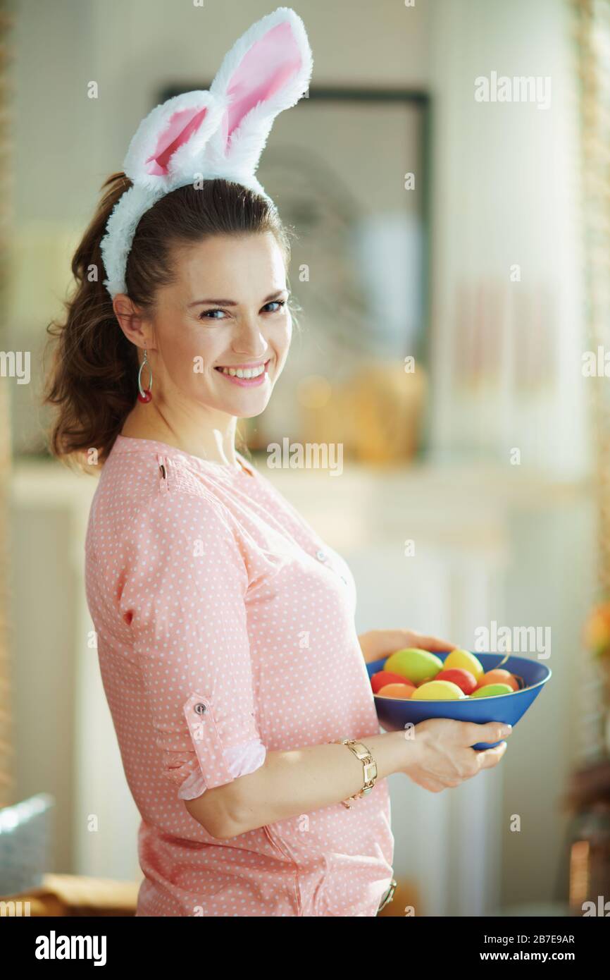 smiling middle age woman in a pink blouse and easter bunny ears holding ...