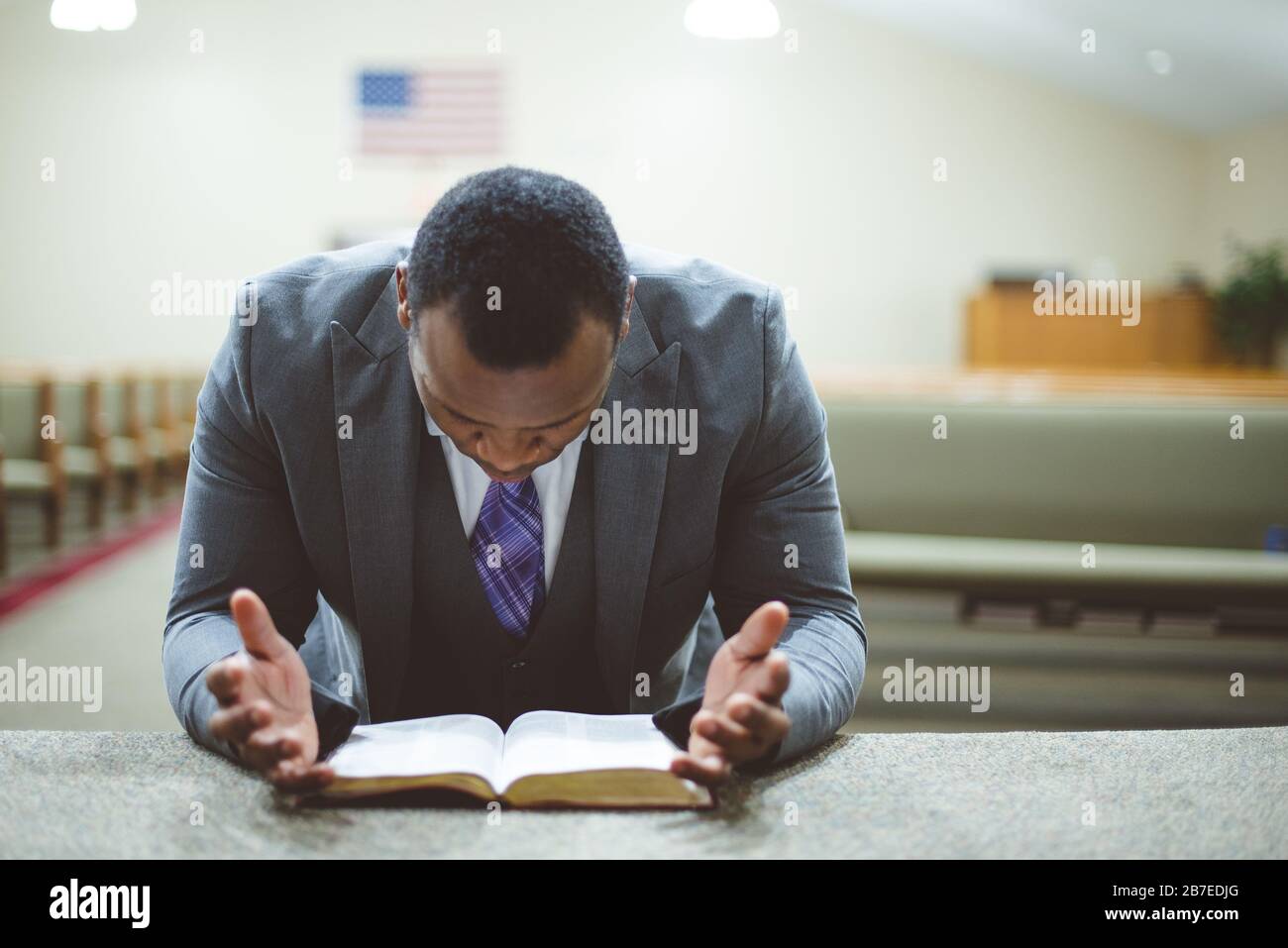 African-American male praying with his head down looking at the Bible ...