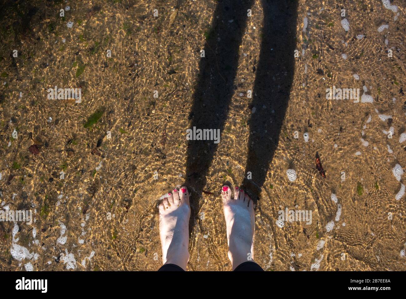 Bare feet with red painted toenails in clear shallow water with leg ...