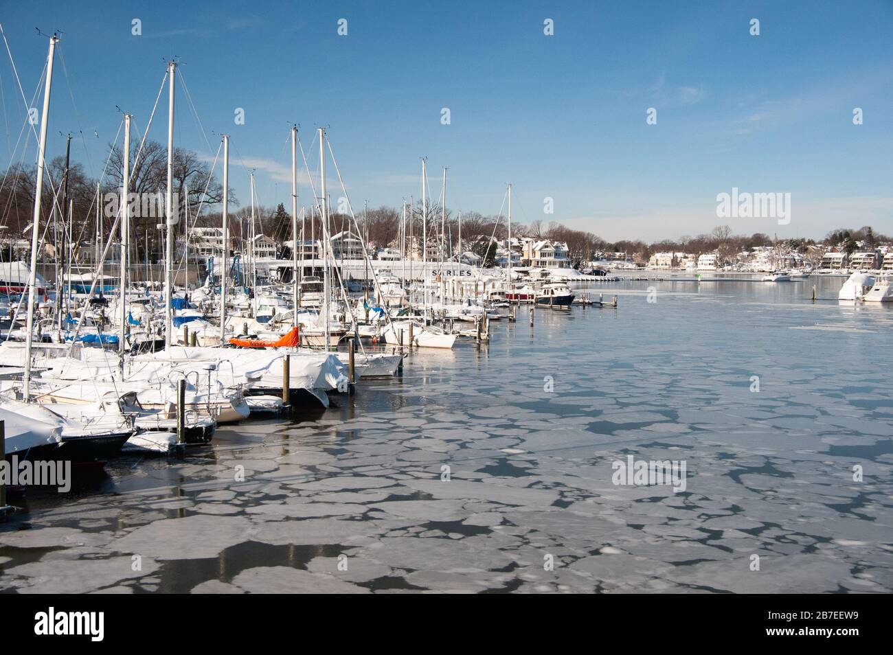 Boats docked at marina on icy river on sunny day after blizzard, with ...