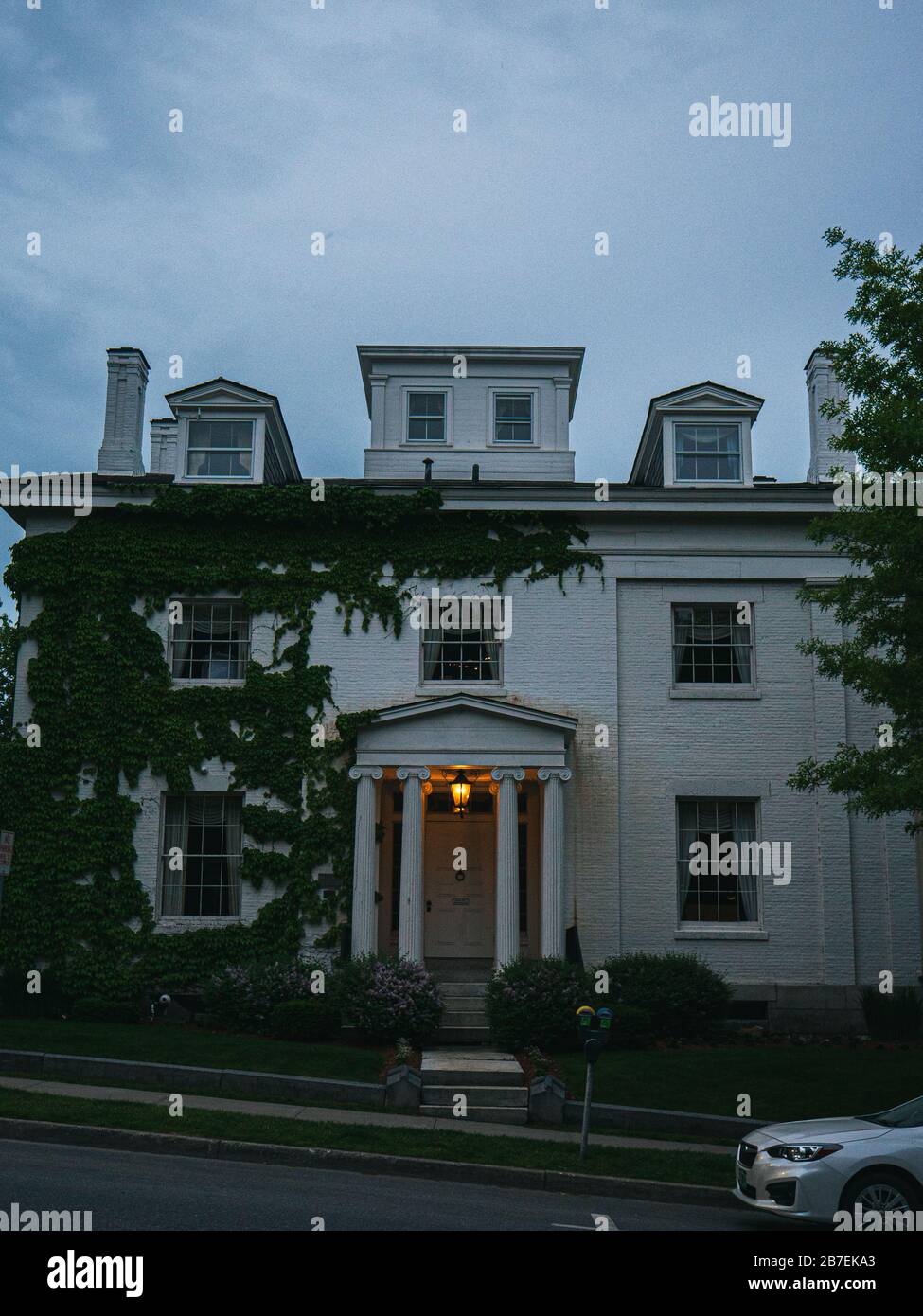 Facade of a mansion house with creeping vines and a lit doorstep light ...