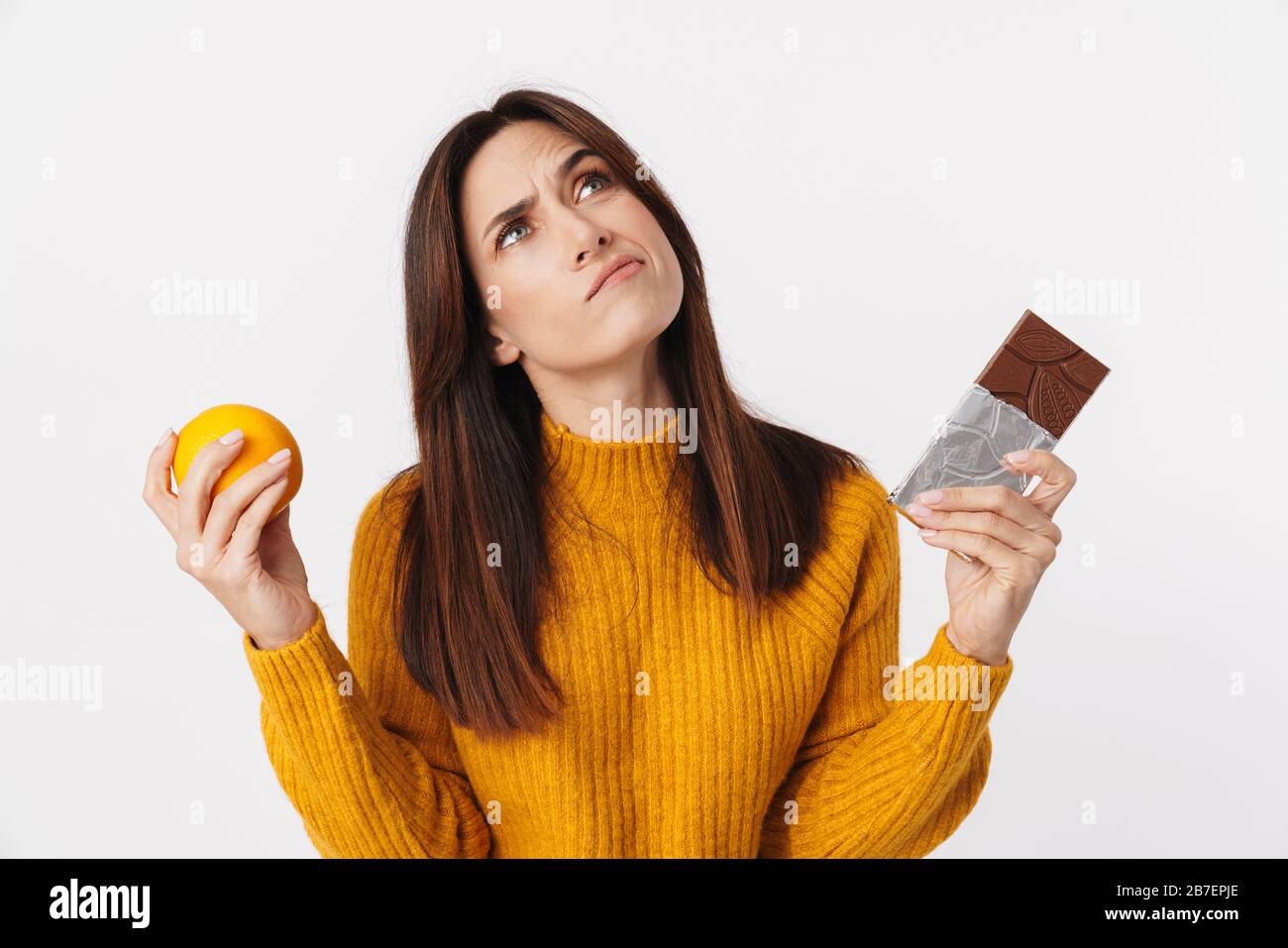 Image of doubtful brunette adult woman hesitating while holding orange ...