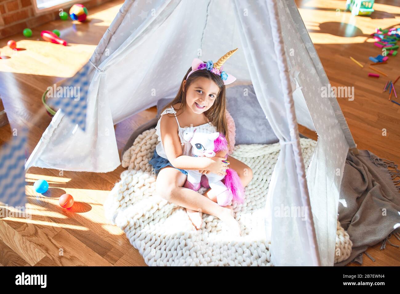 Adorable toddler sitting on the floor inside tipi around lots of toys ...