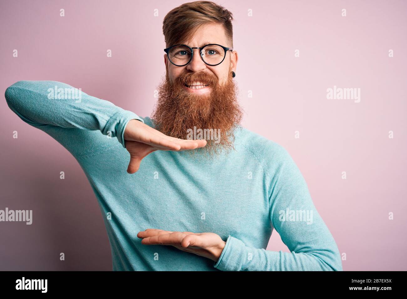 Handsome Irish redhead man with beard wearing glasses over pink ...