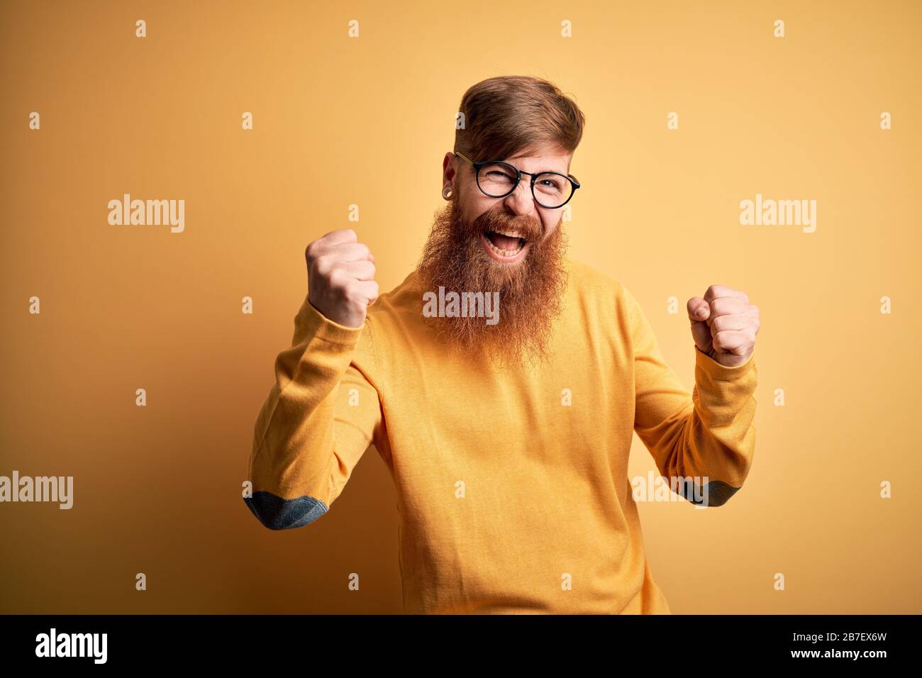 Handsome Irish redhead man with beard wearing glasses over yellow ...