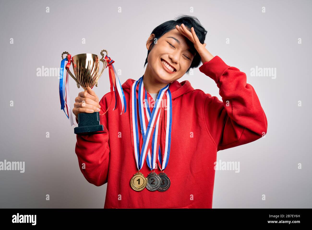 Young beautiful asian girl winner holding trophy wearing medals over ...