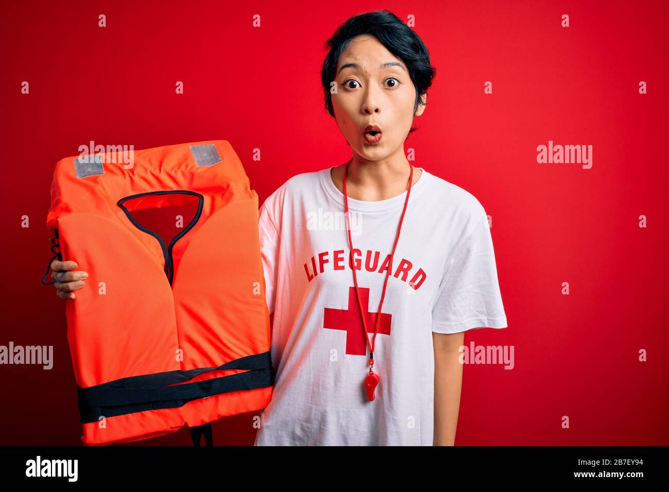 Young beautiful asian lifeguard girl using whistle holding orange life ...