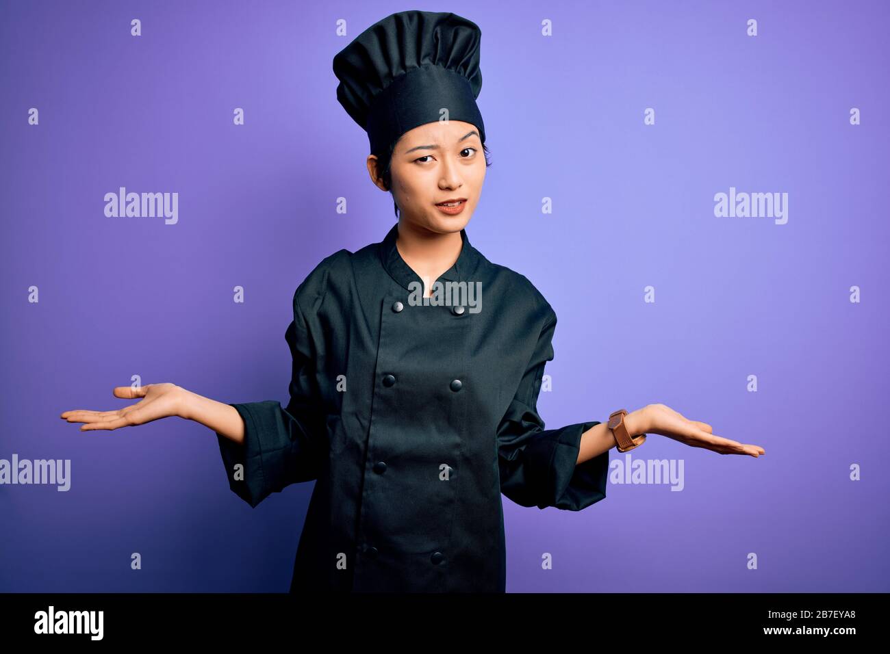 Young beautiful chinese chef woman wearing cooker uniform and hat over ...