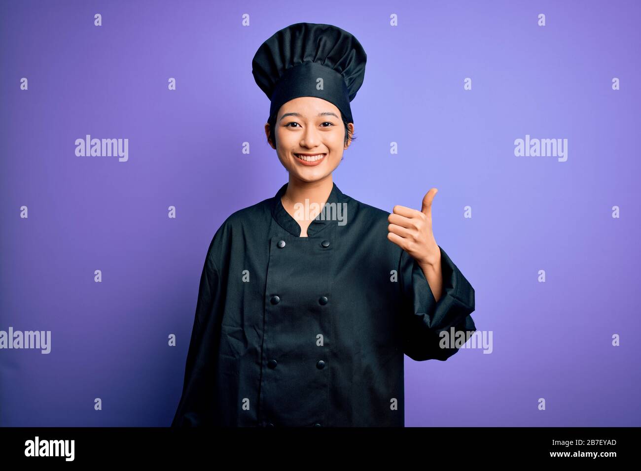 Young beautiful chinese chef woman wearing cooker uniform and hat over ...