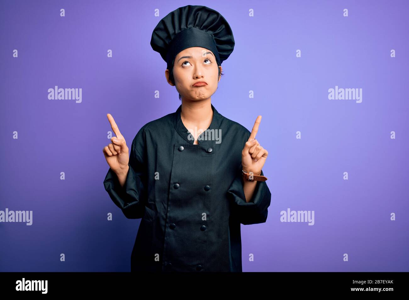 Young beautiful chinese chef woman wearing cooker uniform and hat over ...