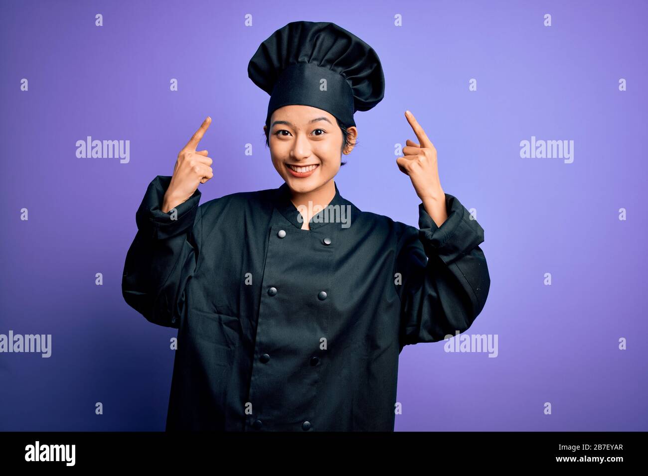 Young beautiful chinese chef woman wearing cooker uniform and hat over ...