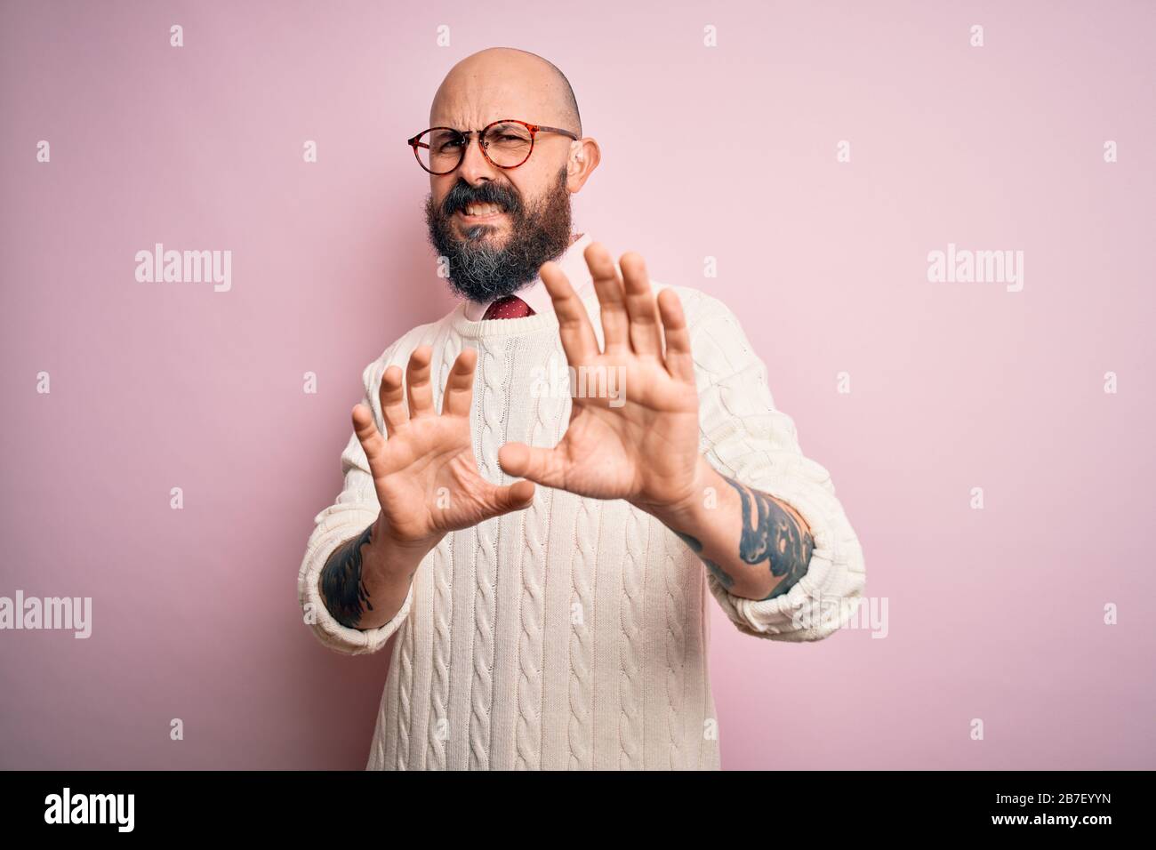 Handsome bald man with beard and tattoo wearing glasses and sweater ...