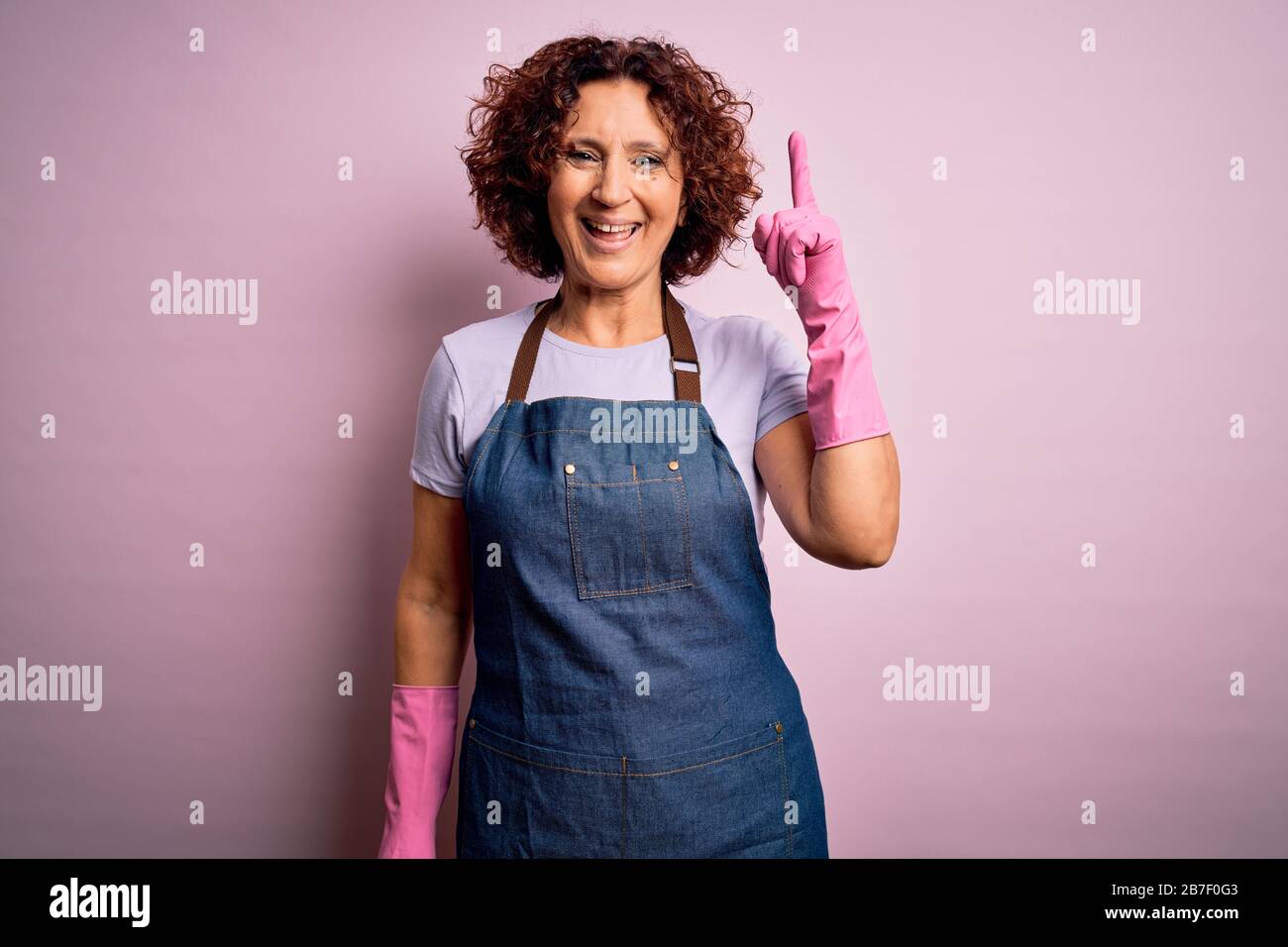 Middle age curly hair woman cleaning doing housework wearing apron and ...