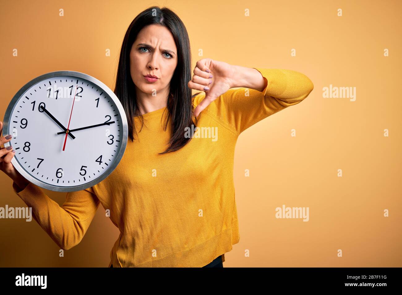 Young woman with blue eyes doing countdown holding big clock over ...