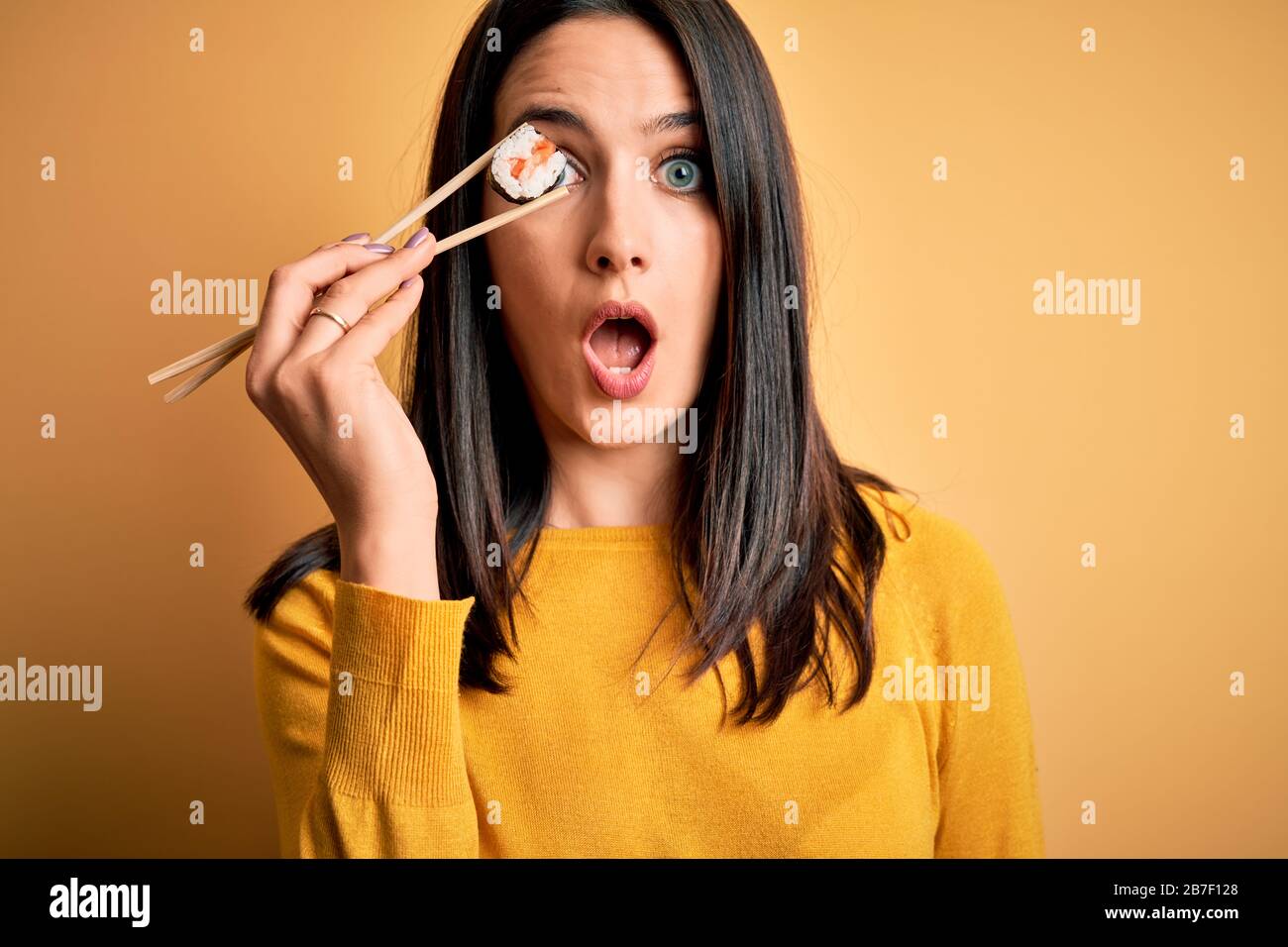 Young brunette woman with blue eyes eating salmon maki sushi using ...