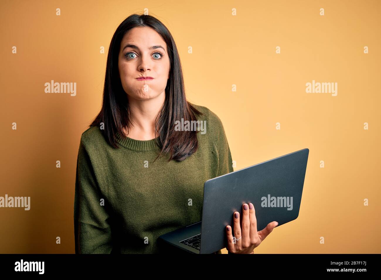 Young brunette woman with blue eyes working using computer laptop over ...