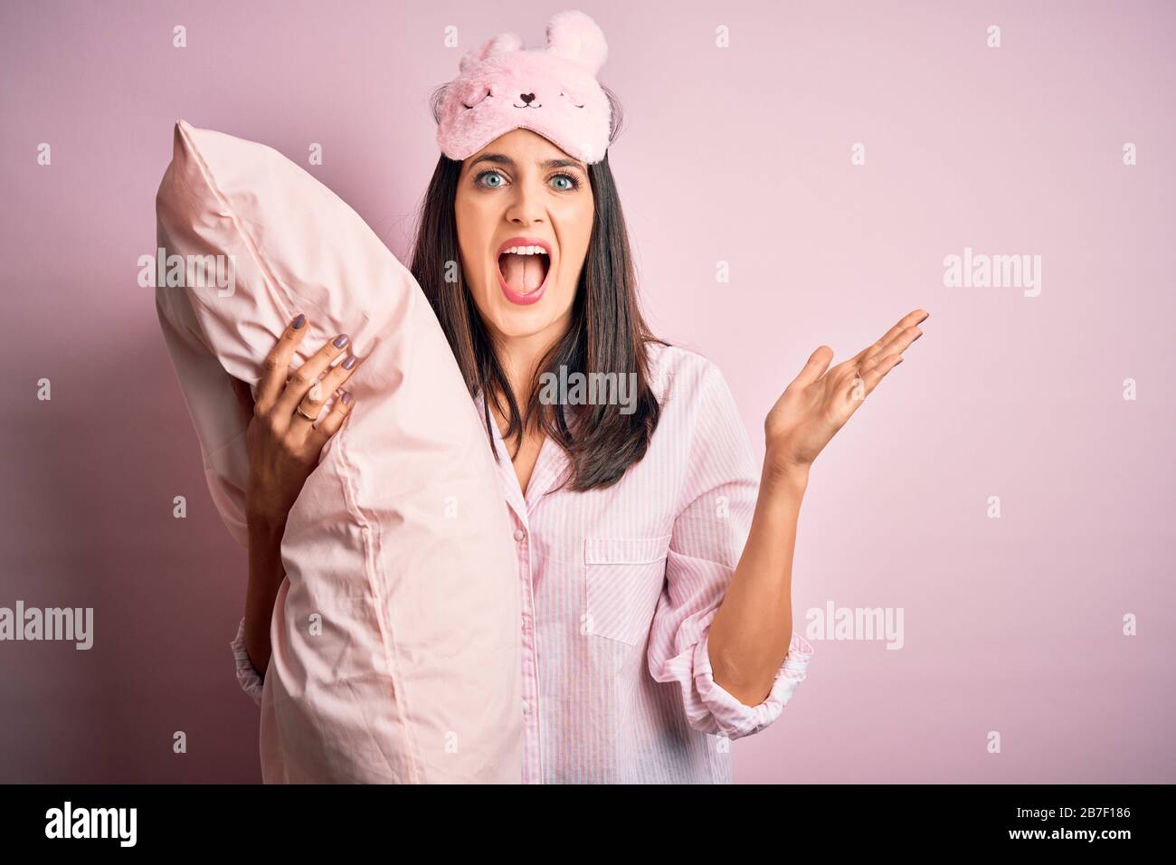 Young brunette woman with blue eyes wearing pajama hugging bed pillow ...
