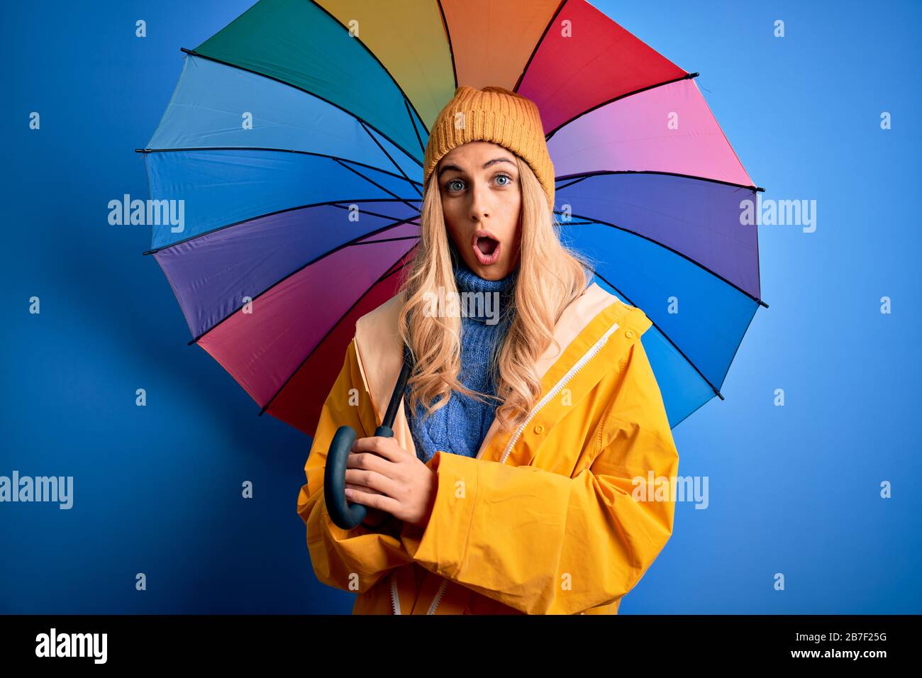 Young beautiful blonde woman wearing raincoat for rainy weather holding ...