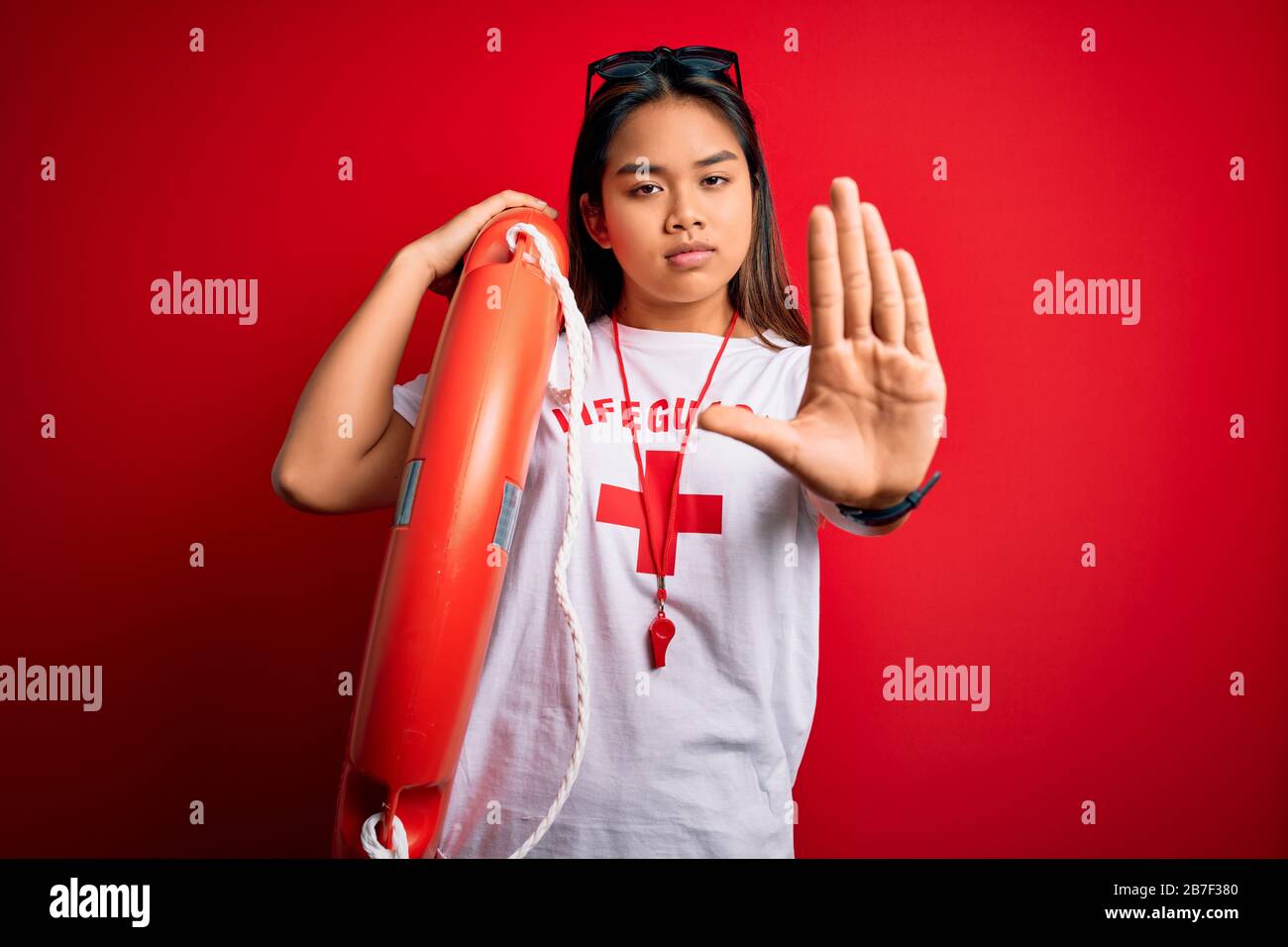 Young asian lifeguard girl wearing t-shirt with red cross using whistle ...