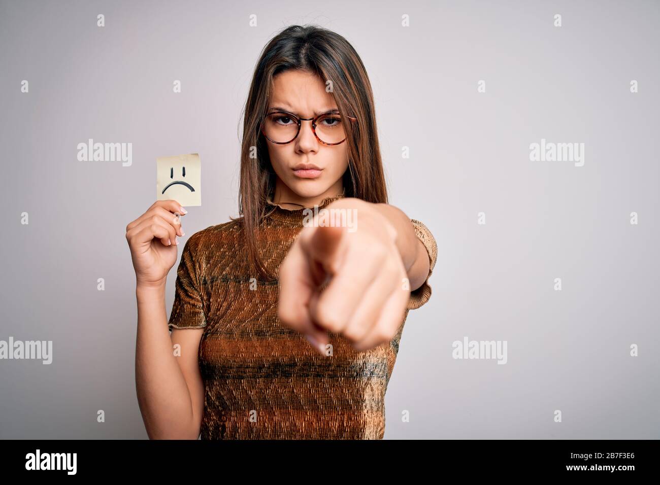 Young beautiful girl holding reminder with sad emotion emoji face over ...
