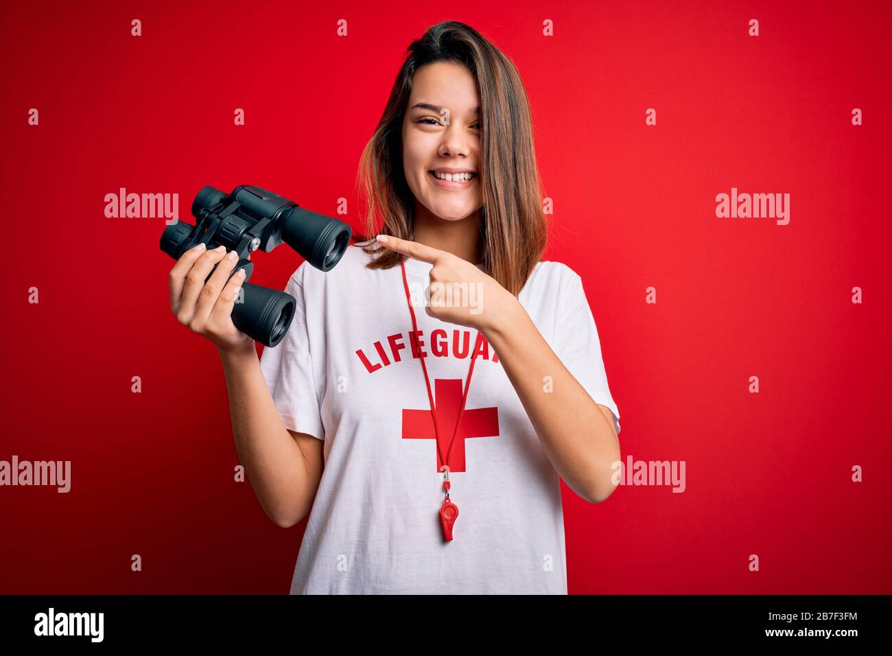 Young beautiful lifeguard girl wearing whistle using binoculars over ...