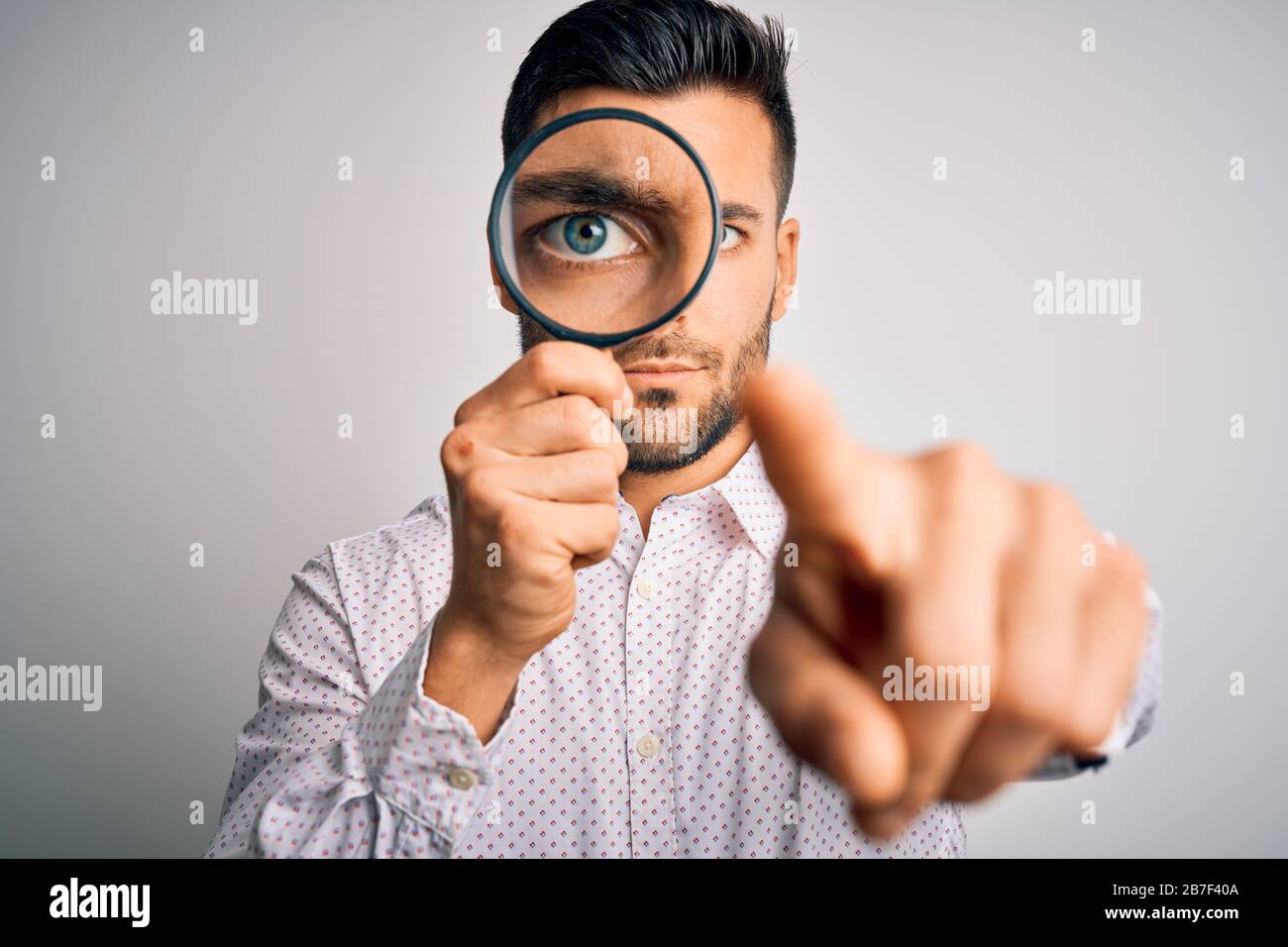 Young detective man looking through magnifying glass over isolated ...